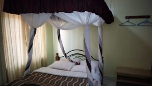 Uma cama de solteiro com dossel, uma mesinha de cabeceira e um cabideiro.