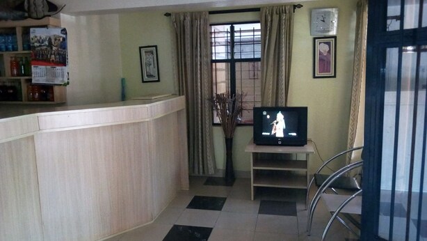Uma sala de estar com televisão, uma mesinha, uma cadeira, uma janela com cortinas e um relógio na parede.