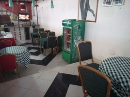 Um restaurante com toalhas de mesa xadrez, cadeiras verdes, uma máquina de refrigerantes Sprite verde e uma televisão ao fundo.