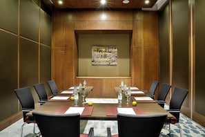 Uma sala de conferência com uma mesa comprida, cadeiras pretas, garrafas de água e um quadro na parede.