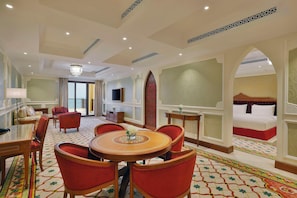 Quarto de hotel com área de jantar, televisão, cama e vista para o exterior.