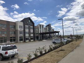 Um hotel MainStay Suites com design moderno, estacionamento e céu claro.