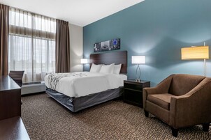 Quarto de hotel com cama, escrivaninha, cadeira e mesa de cabeceira com luminárias.