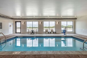 Piscina interna com paredes de vidro transparente, chão ladrilhado e vista para o exterior.