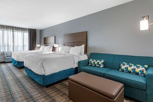 Quarto de hotel com duas camas, um sofá e uma pequena mesa.
