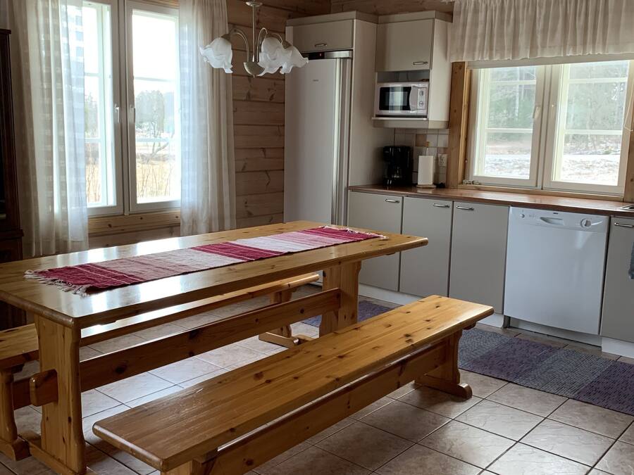 Interior em madeira com cozinha, incluindo mesa de madeira com bancos, micro-ondas e geladeira.