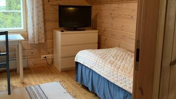 Um quarto aconchegante com teto inclinado, uma cama com colcha azul e branca, cômoda, televisão sobre suporte e janela com cortinas.
