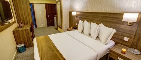 Quarto de hotel com uma cama grande, uma mesa de cabeceira com abajur, um espelho e uma televisão em um suporte.