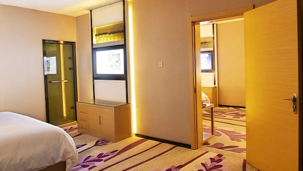 Quarto de hotel com cama, espelho, guarda-roupa e porta que dá para outro cômodo.