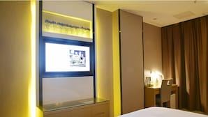 Quarto de hotel com cama, escrivaninha, cadeira e janela com vista para um edifício.