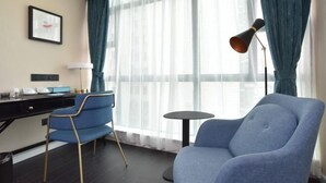 Quarto de hotel com escrivaninha, duas cadeiras, uma mesa redonda pequena e um abajur.