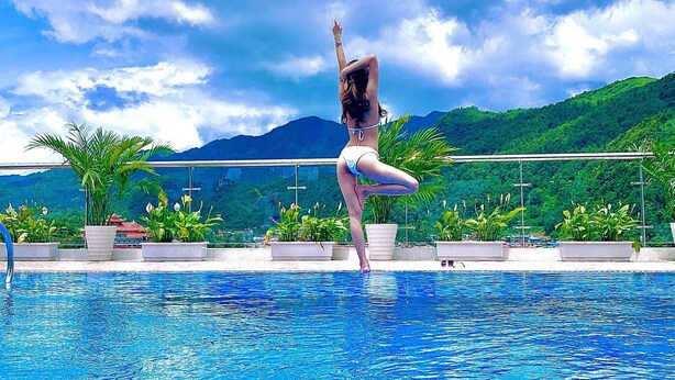 Uma pessoa pula numa piscina de natação, com uma paisagem montanhosa ao fundo.