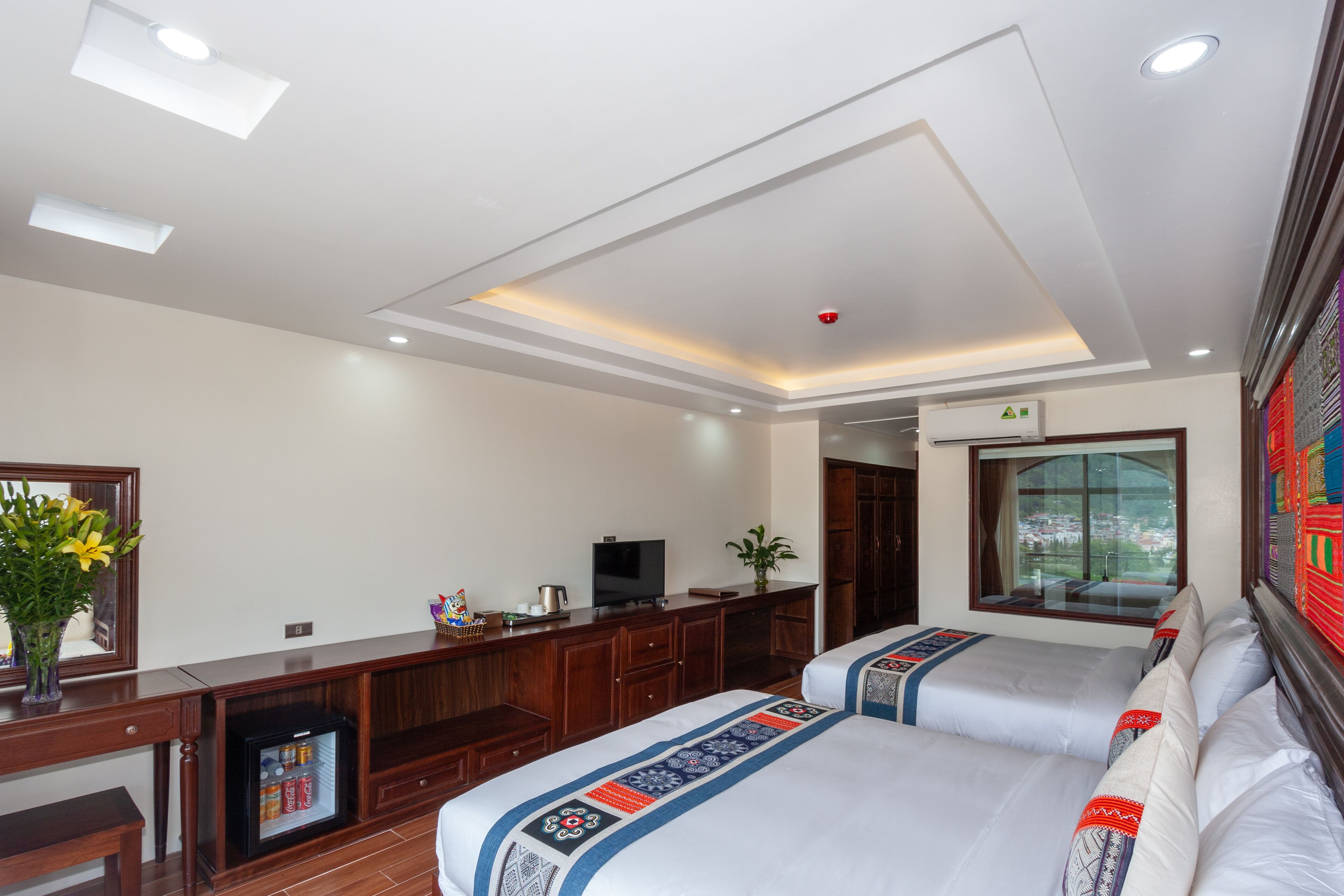 Quarto de hotel com duas camas, uma escrivaninha com televisão, um mini-frigobar e uma janela com vista para a cidade.