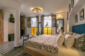 Quarto de hotel com cama, poltrona, mesa e vista para o exterior pela janela.