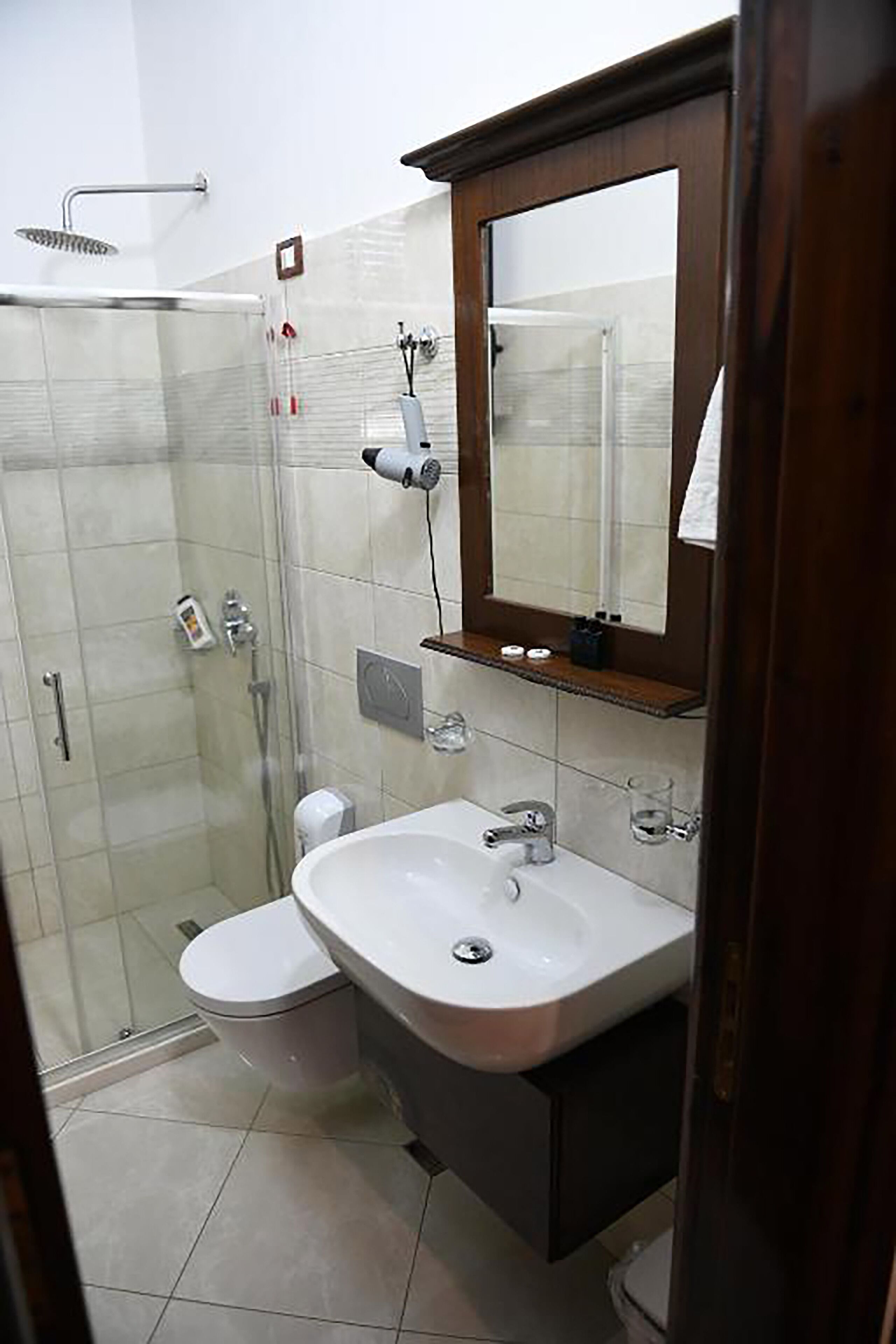 Um banheiro com box de vidro, vaso sanitário branco e pia com espelho acima.