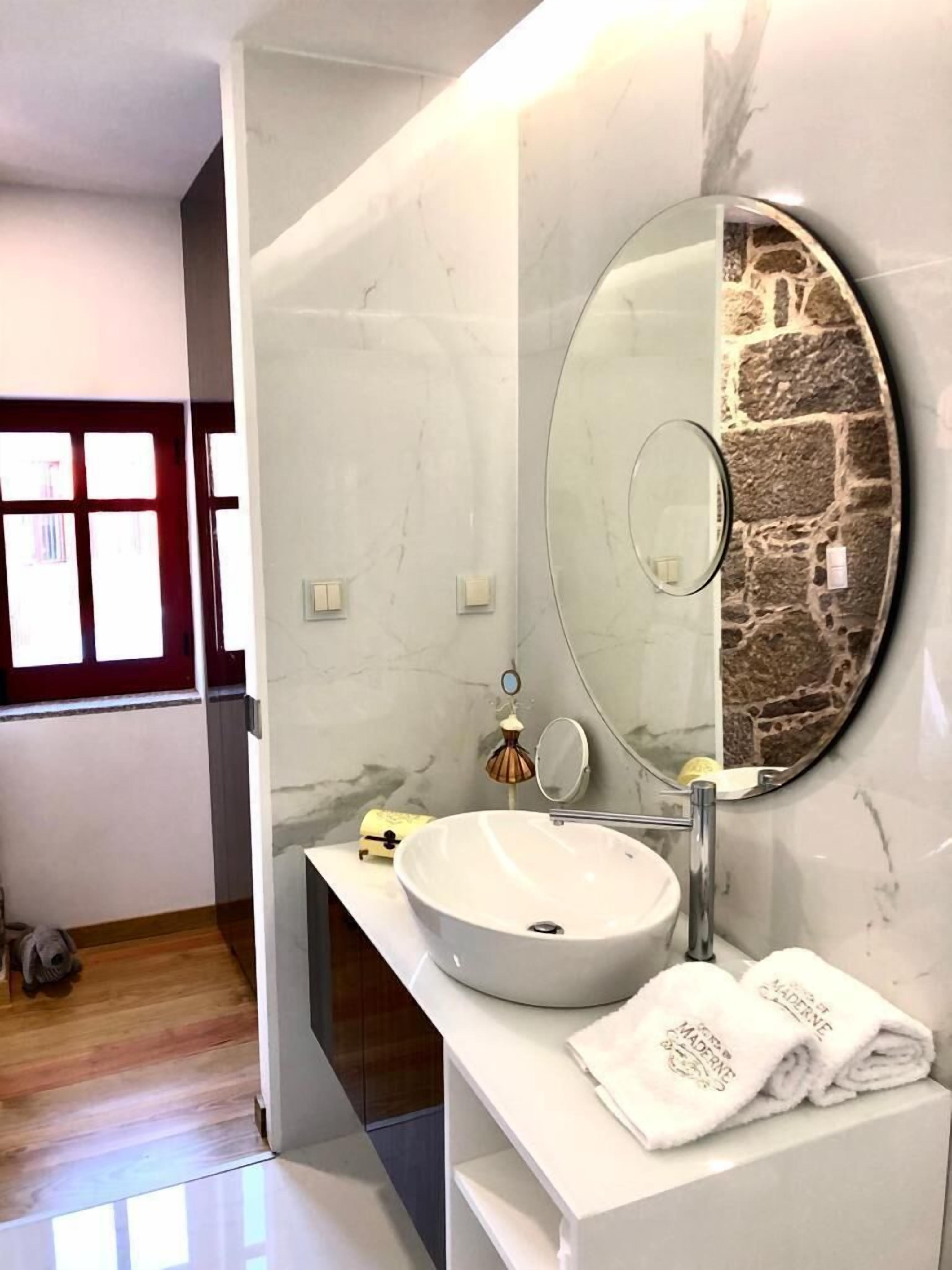 Uma casa de banho moderna com uma pia branca, um espelho grande e um porta-toalhas.