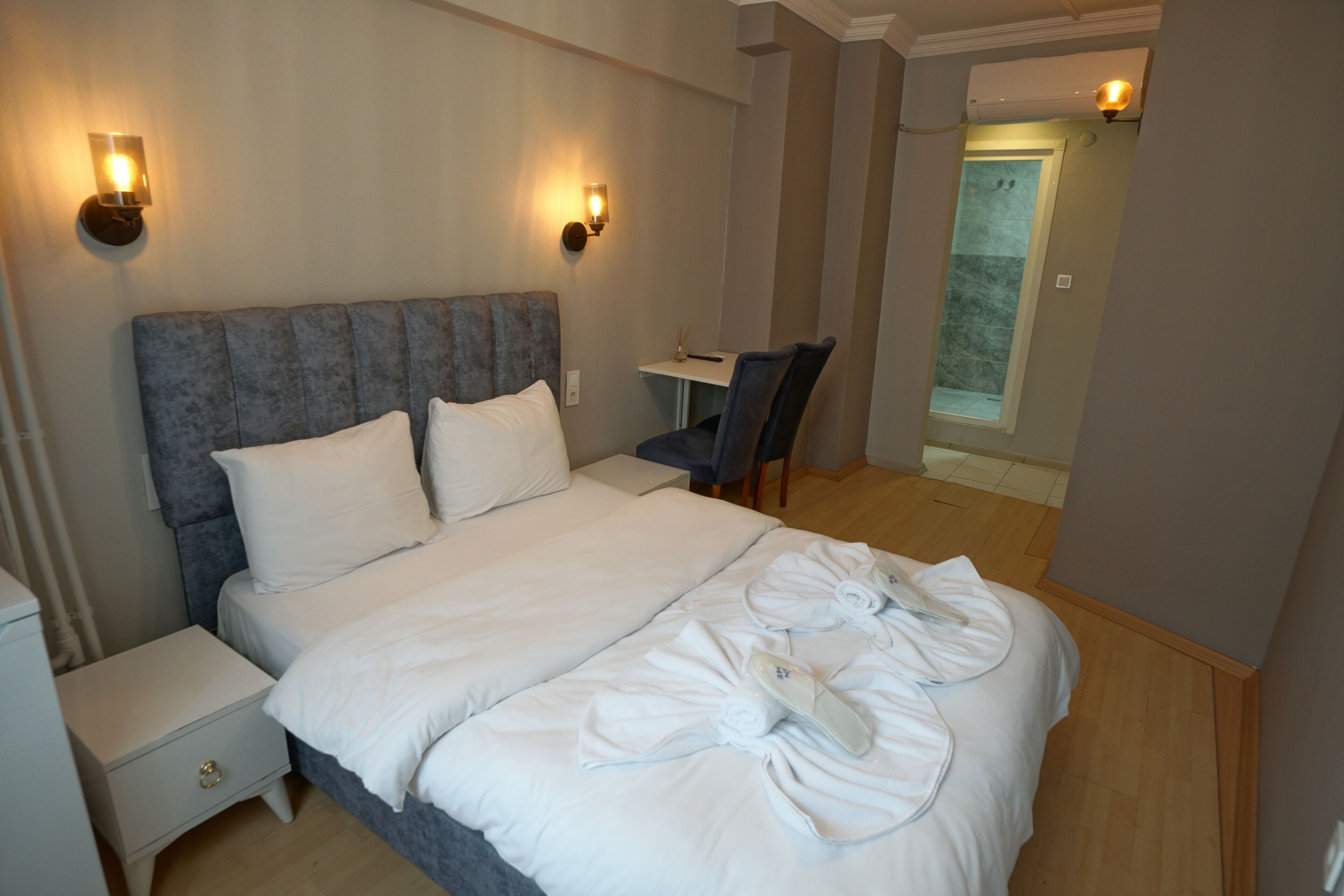 Quarto de hotel com uma cama grande, duas mesas de cabeceira, uma escrivaninha e uma cadeira.