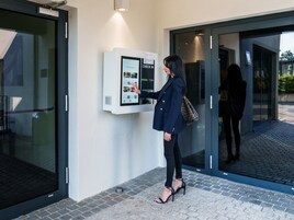 Mulher a interagir com um quiosque de check-in digital na entrada de um hotel.