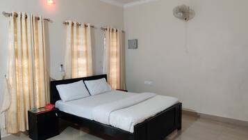 Quarto com cama, cortinas, mesa de cabeceira, tomada na parede e ventilador de teto.