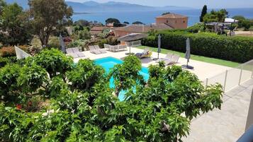 Área de piscina com espreguiçadeiras e guarda-sóis, cercada por vegetação exuberante e vista para o mar e montanhas.