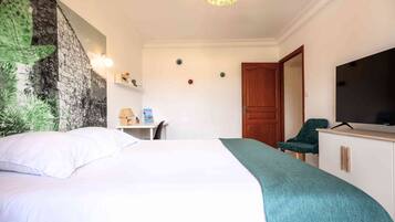 Quarto de hotel com cama, escrivaninha, cadeira, televisão e guarda-roupa.