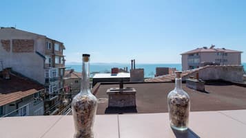 Duas garrafas de vidro com conchas em um terraço com vista para uma paisagem urbana costeira.