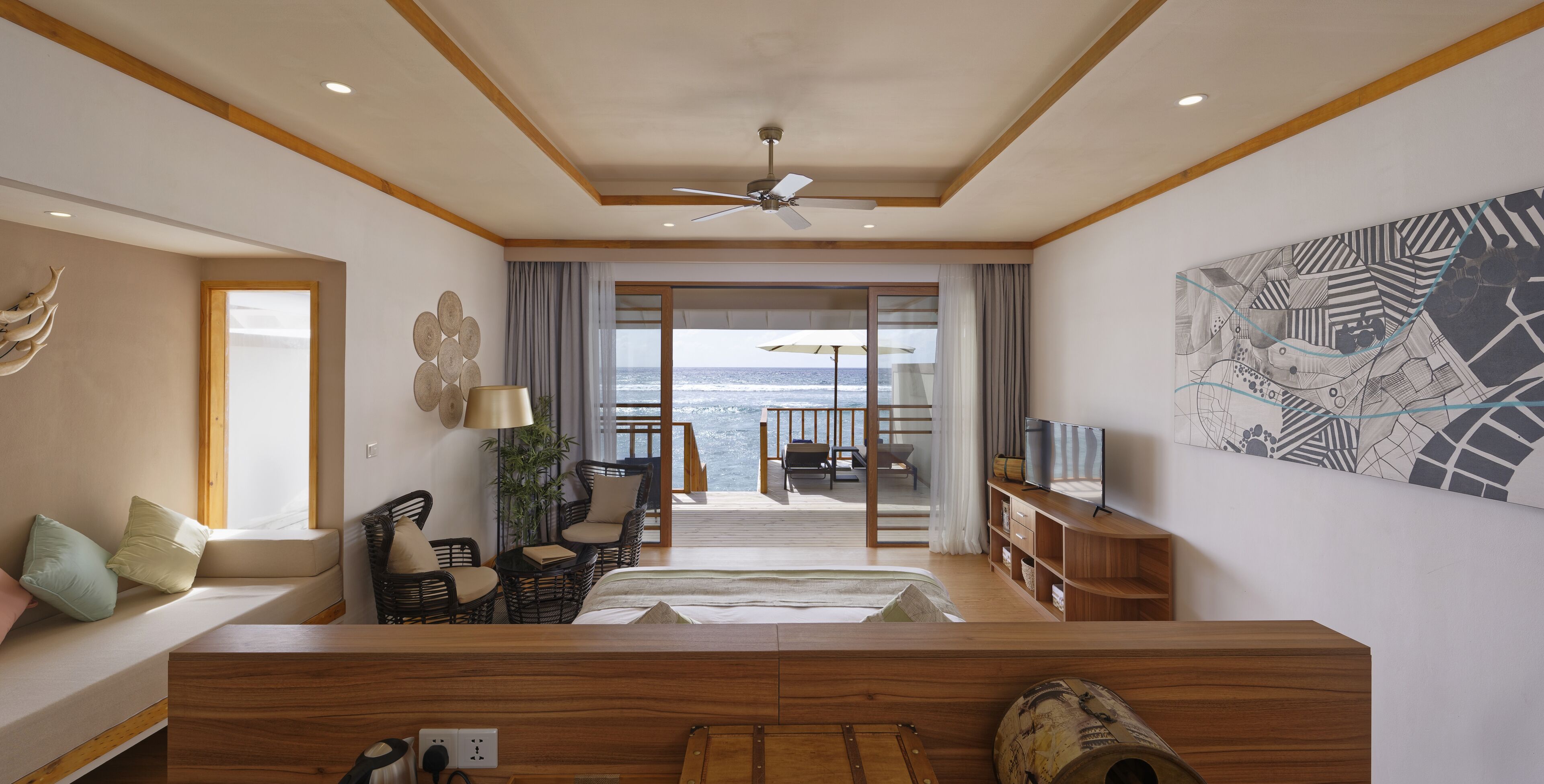 Quarto de hotel moderno com uma cama grande, área de estar com vista, televisão e varanda com vista para o mar.