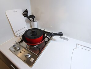 Cozinha com uma panela vermelha em um fogão a gás, bancada branca e parede branca.
