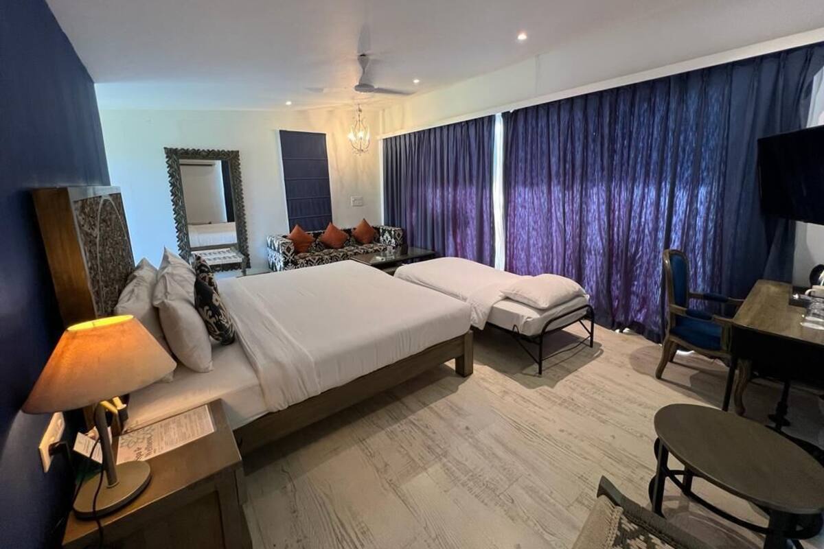 Quarto de hotel com duas camas, uma escrivaninha, uma cadeira, uma televisão e um candelabro.