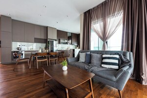 Uma sala de estar moderna com um sofá, mesa de centro e uma área de jantar com cadeiras, além de uma cozinha ao fundo.