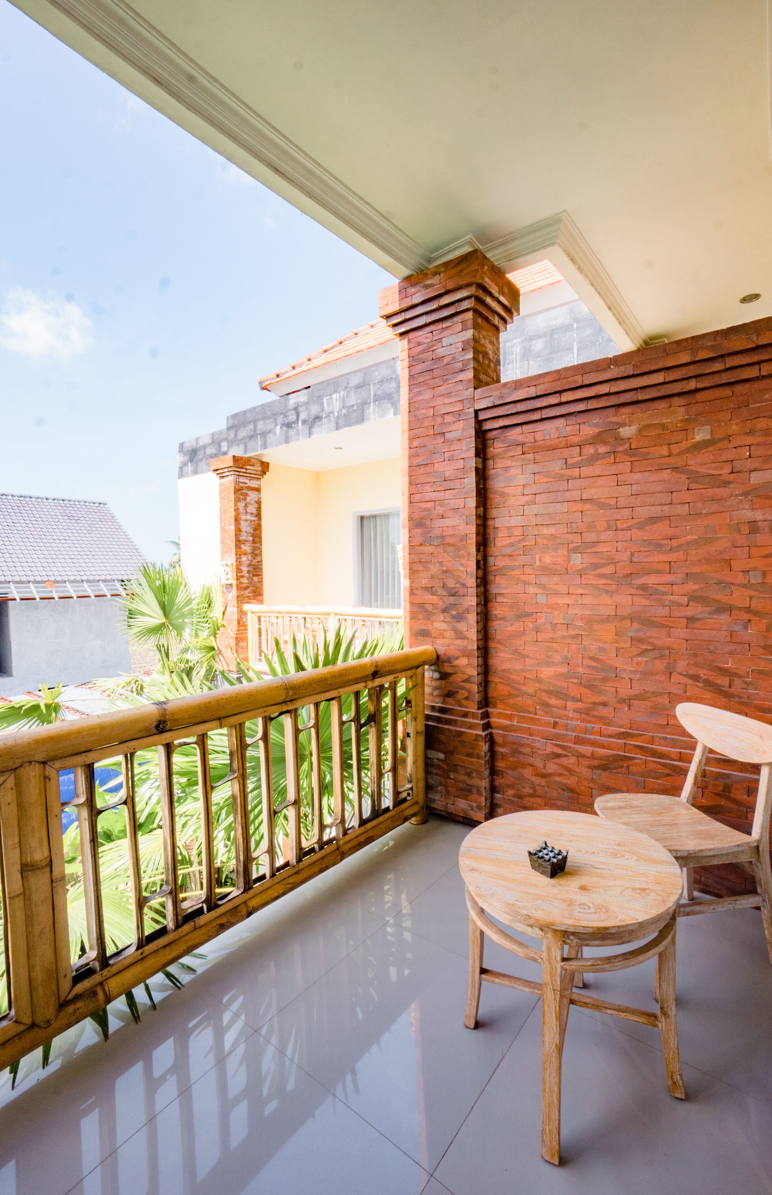 Uma varanda com piso de azulejos, duas cadeiras de madeira, uma mesa pequena e um muro de tijolos.