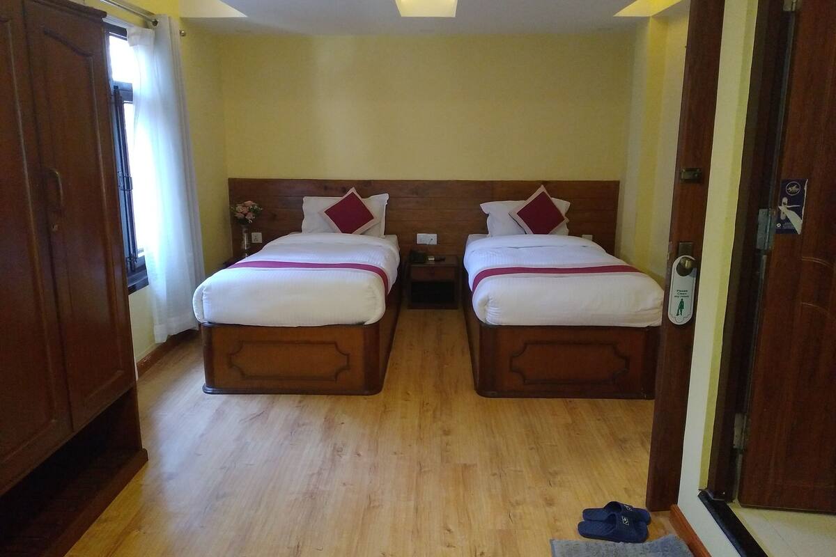 Quarto de hotel com duas camas, cabeceiras de madeira, um guarda-roupa de madeira e um tapete pequeno no chão.