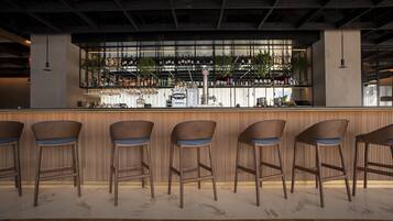 Uma área de bar com banquetas de madeira e uma estante cheia de garrafas.