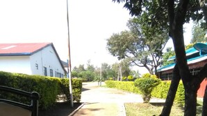Uma passagem leva a um edifício com telhado vermelho, cercado por vegetação e uma antena parabólica.