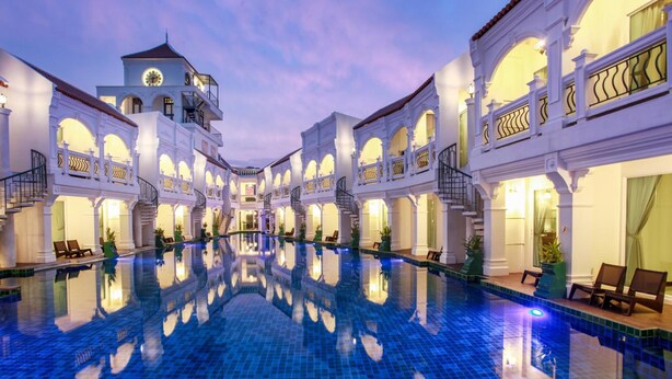 Um hotel luxuoso com piscina central, várias varandas e um campanário.