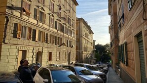 Rua estreita com carros estacionados e edifícios históricos com várias janelas e varandas.