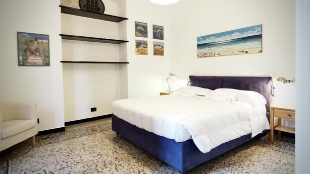 Um quarto com cama, cadeira, escrivaninha e prateleiras.