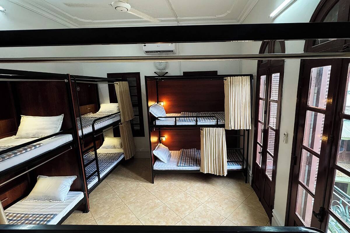 Um vagão de trem com beliches, uma janela com cortinas e piso de azulejos.