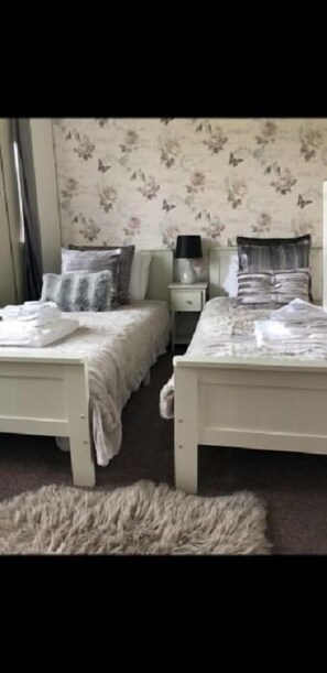 Quarto com duas camas, uma mesa de cabeceira, um abajur e papel de parede floral.