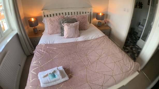 Quarto com cama grande, duas luminárias de cabeceira, um quadro na parede e uma janela com cortinas.