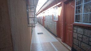 Um corredor com piso de azulejos, portas vermelhas e janelas com grades de metal.