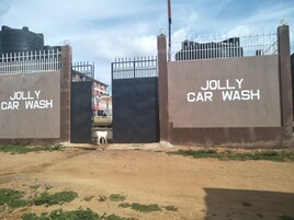 Uma entrada gradeada para uma lavagem de carros chamada 'Jolly Car Wash', com um caminho de terra que leva à entrada.