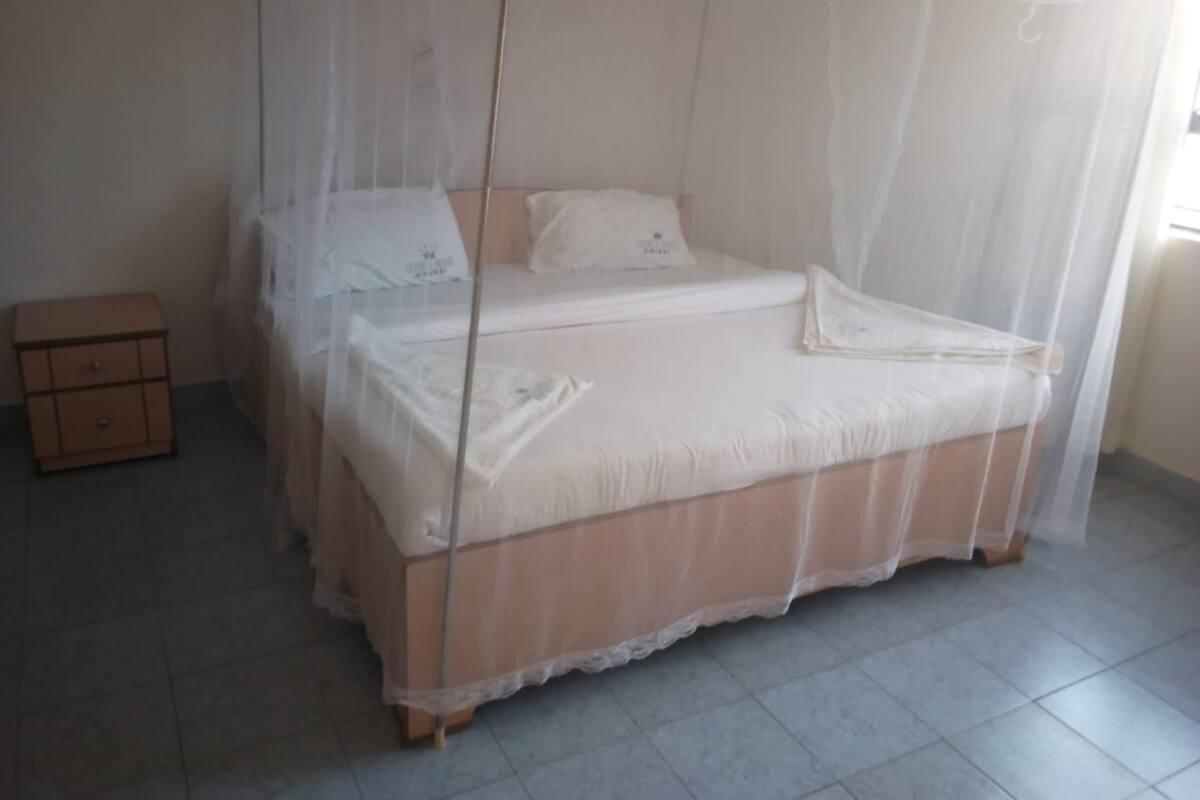 Uma cama de solteiro com dossel, mesa de cabeceira e janela com cortinas.