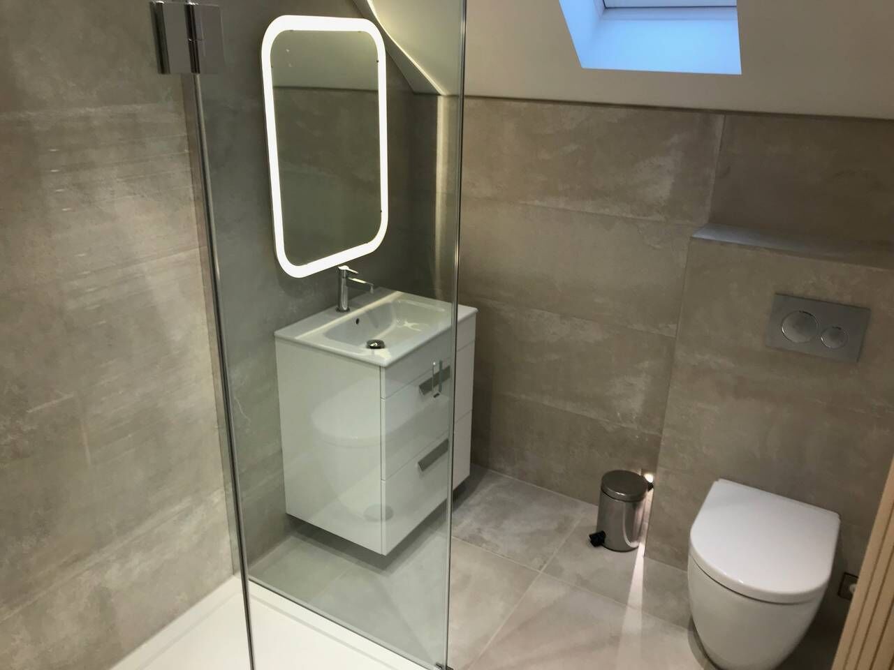Uma casa de banho moderna com cabine de duche em vidro, lavatório branco e sanita.