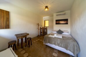 Quarto com cama, escrivaninha, banquinhos, cadeira e um quadro na parede.