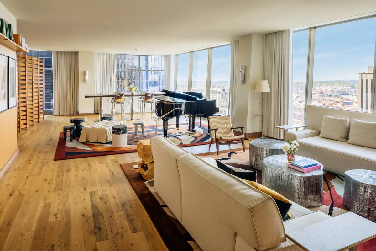 Uma sala de estar ampla com um piano de cauda, um sofá e vista para a cidade através de grandes janelas.