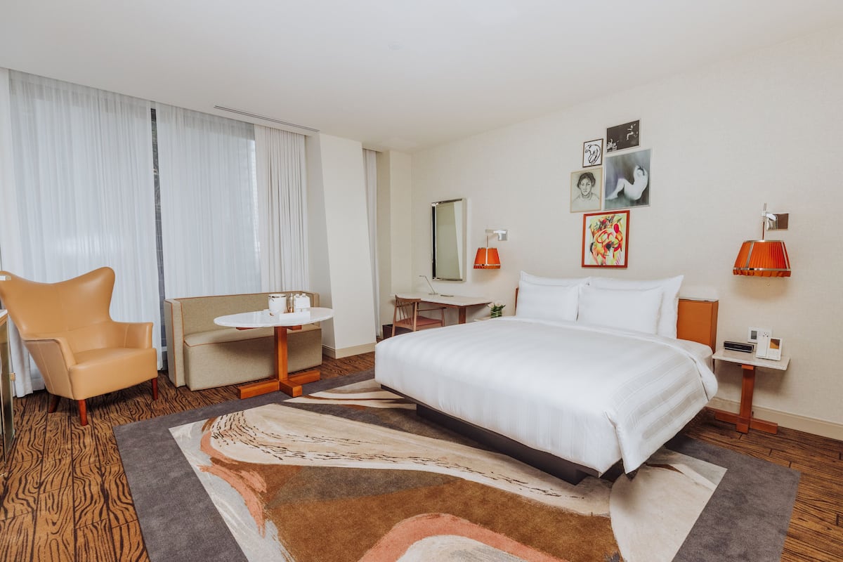 Quarto de hotel com uma cama grande, uma escrivaninha, uma cadeira, uma mesinha e um espelho.