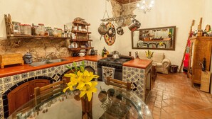 Cozinha com painel de azulejos, armários de madeira, fogão e área de jantar com mesa e cadeiras de vidro.