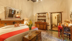 Quarto com uma cama grande, cabeceira de madeira, espelho, um vaso com flores, mesa de cabeceira de madeira e uma cadeira vermelha.