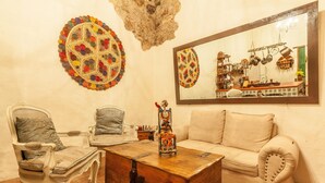 Uma sala de estar com uma mesa de centro de madeira, duas poltronas, um sofá e um espelho grande que reflete o ambiente.